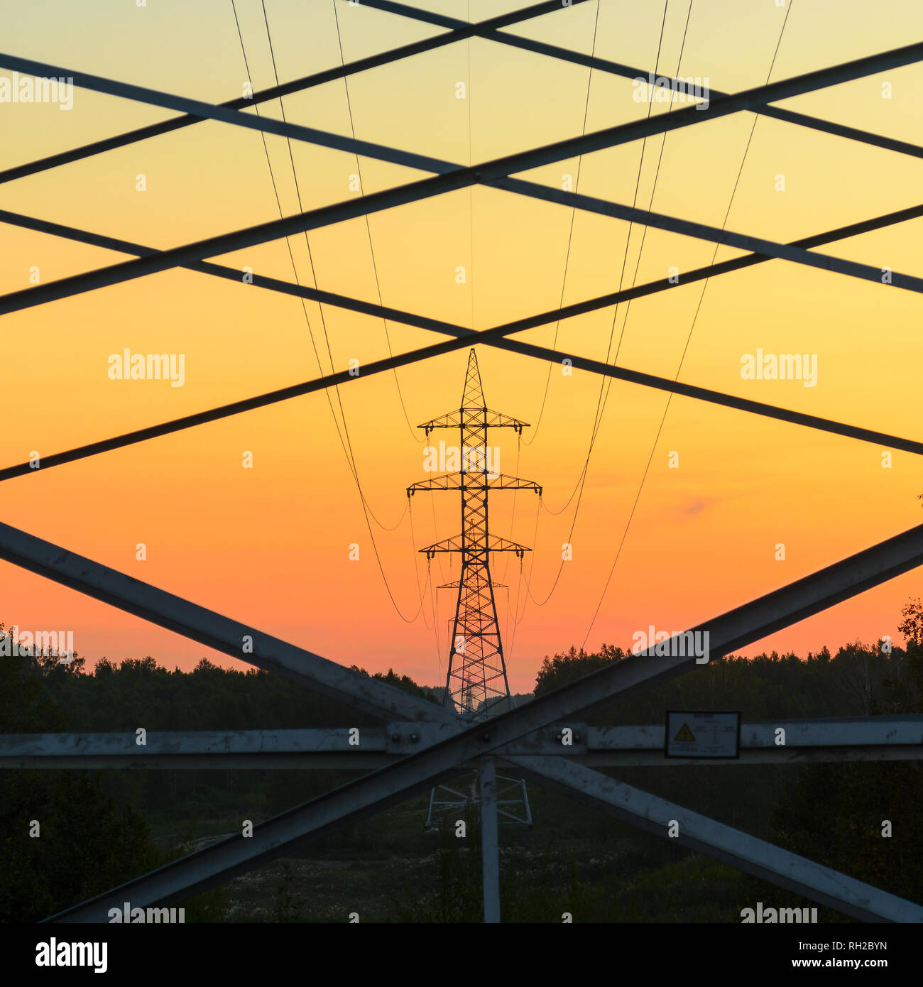 Power line pylons with wires against a sunset orange sky and forest ...