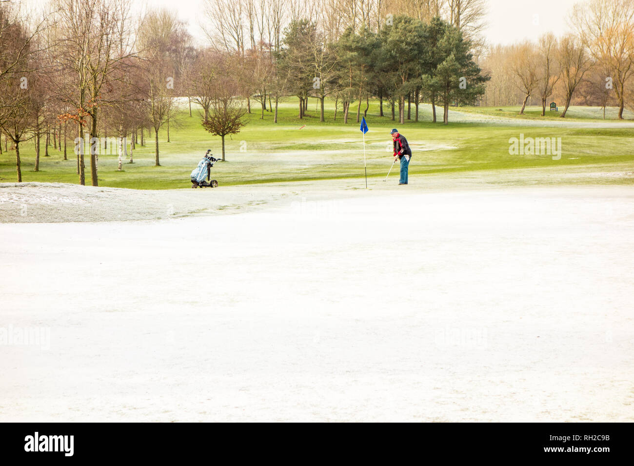 Man playing golf in winter on golf a course despite snow and freezing ...