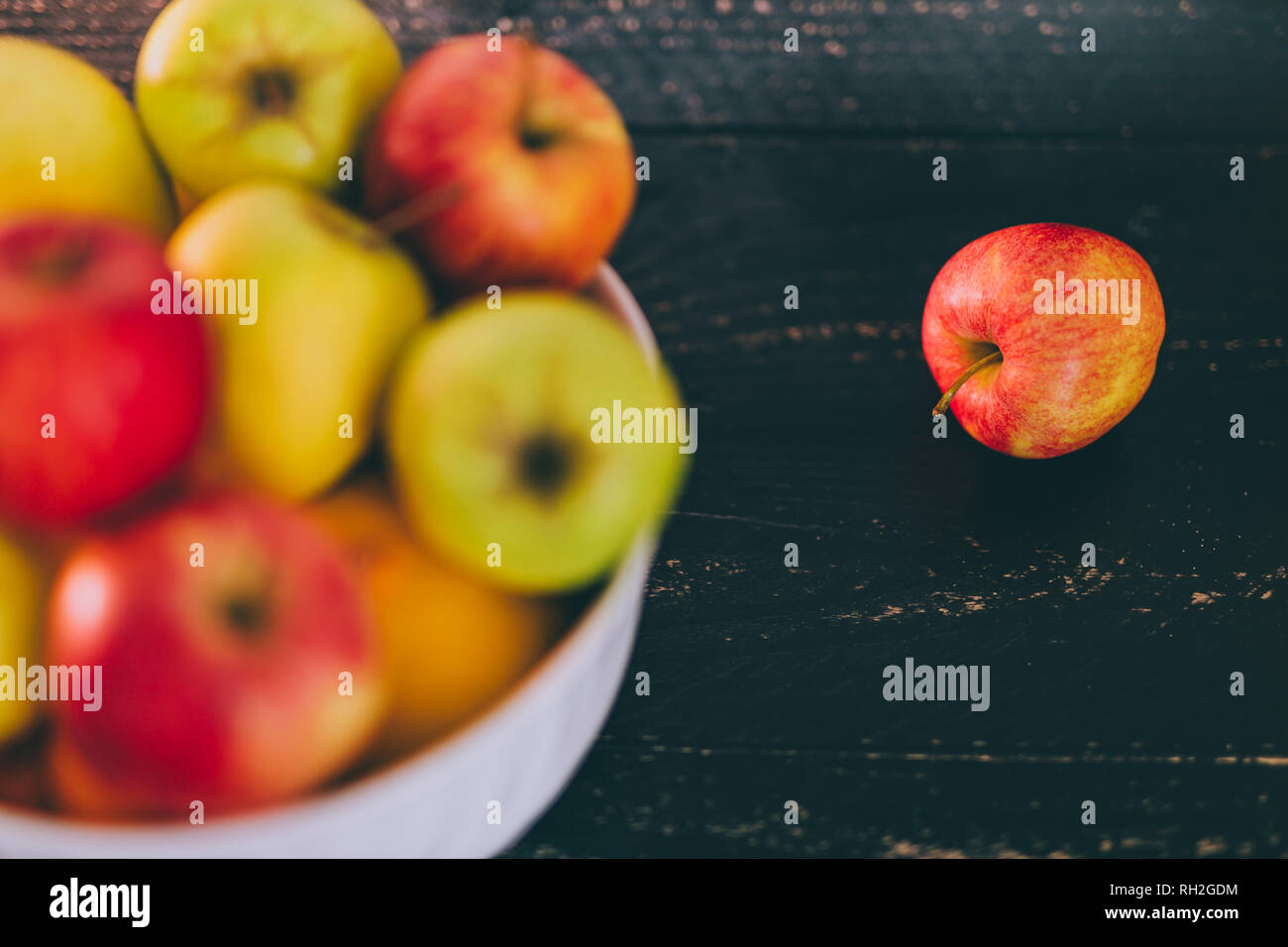 group of mixed red green and yellow apples in a white bowl on dark wood ...