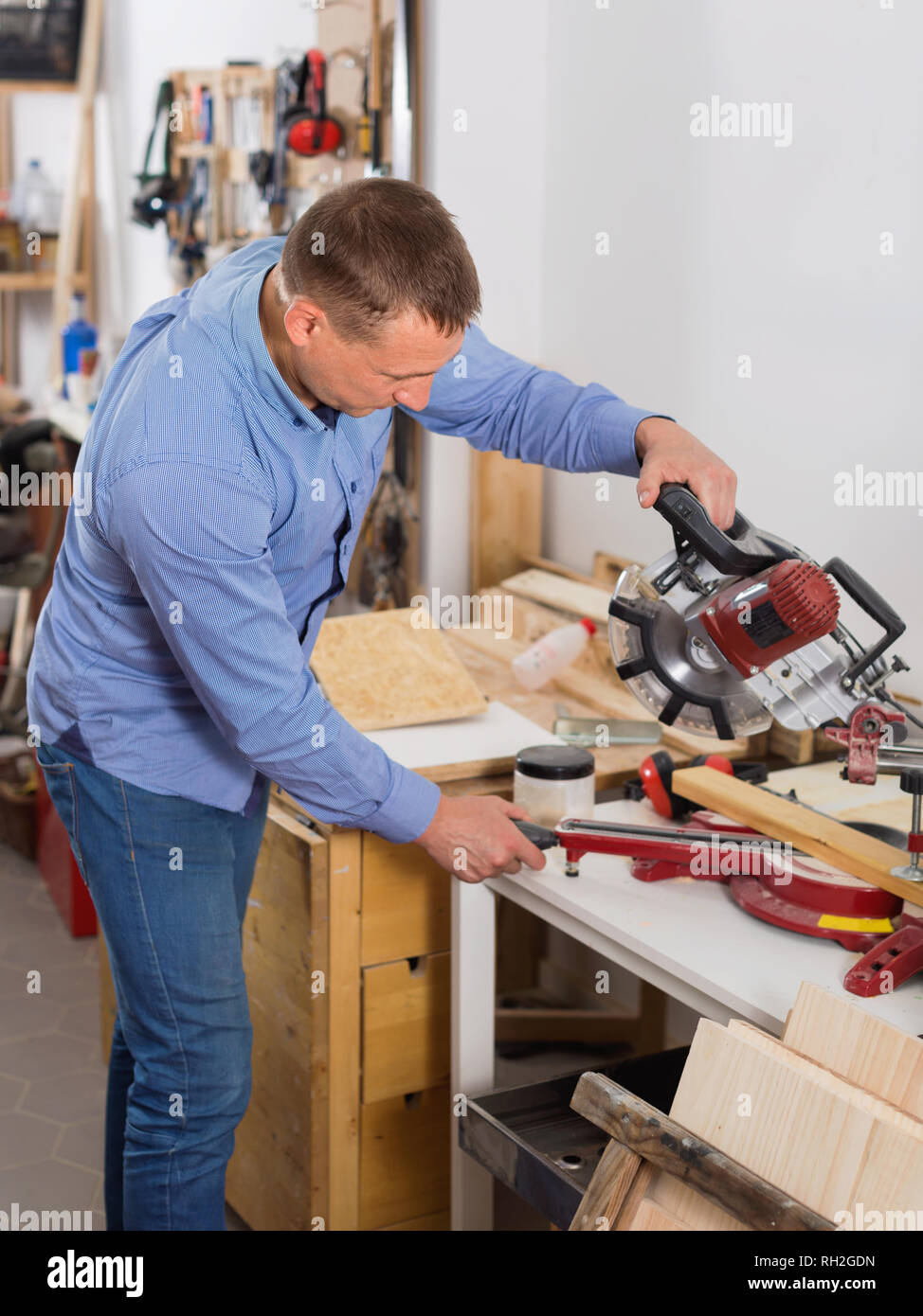 Young woodworker male cutting wooden plank with fret saw in workplace ...