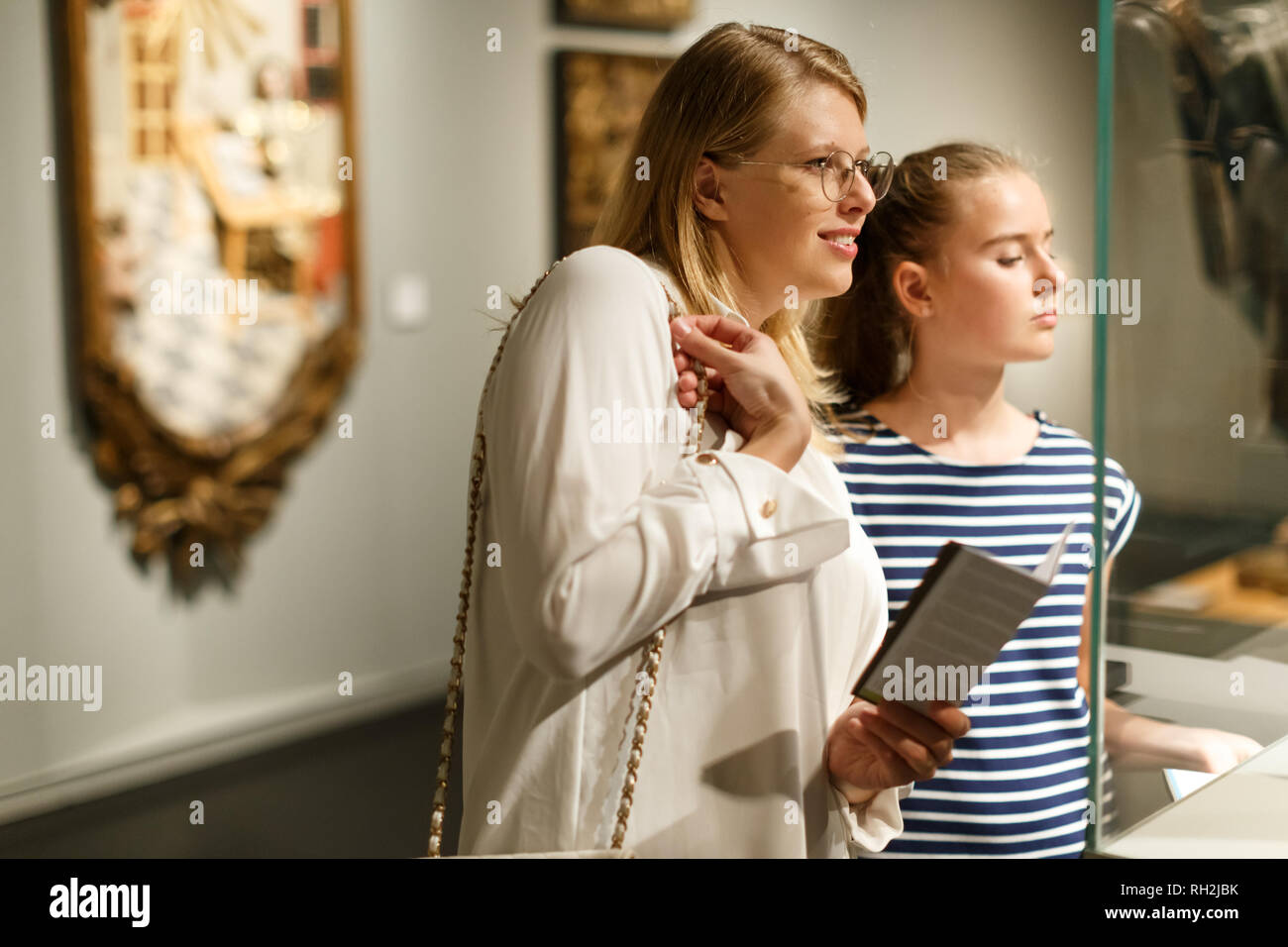 Girl with woman looking with interest at art objects in museum, using ...