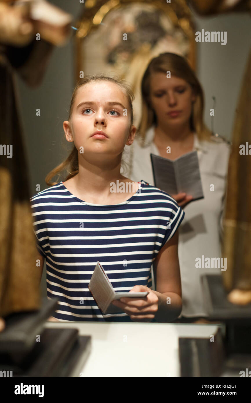Girl looking at art objects in museum and using guidebook, mother on ...