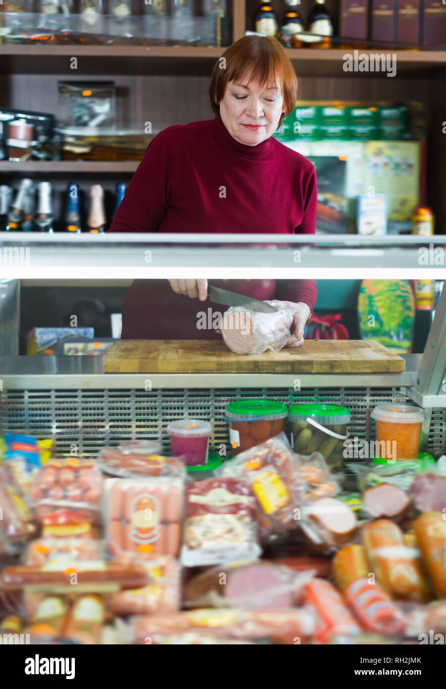 Smiling female selling sausage and ham at the counter in supermarket ...