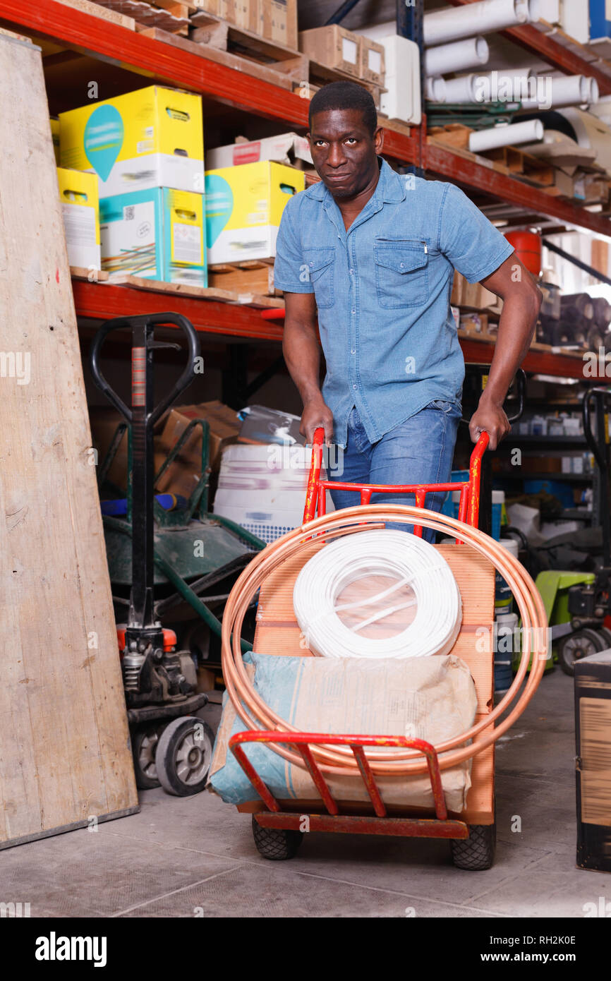 Focused African American diligent cheerful smiling carrying handbarrow ...