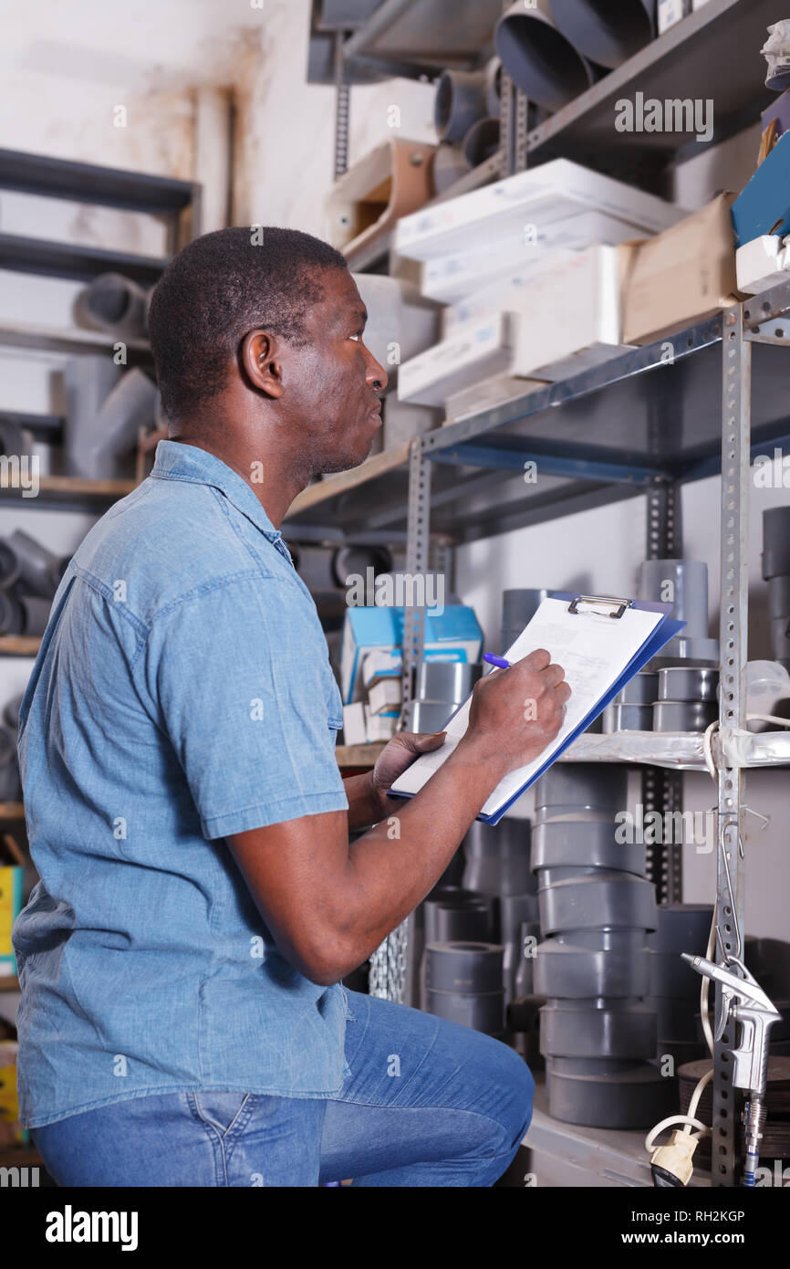 Happy African American male warehouse worker making notes while ...
