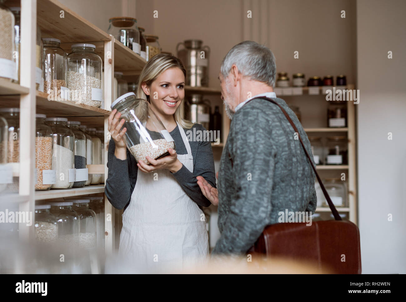 Young female shop assistant serving a senior man customer in a zero ...