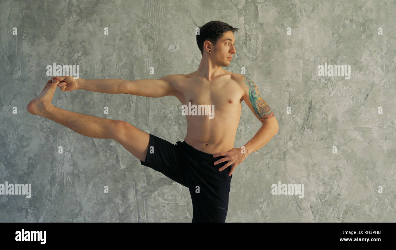 Male yoga master stretching leg in the studio. Standing, holding Stock ...