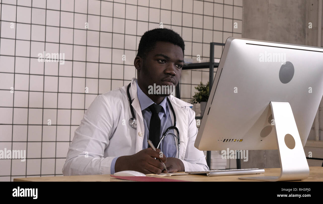 Young african-american doctor making notes and looking up something on ...