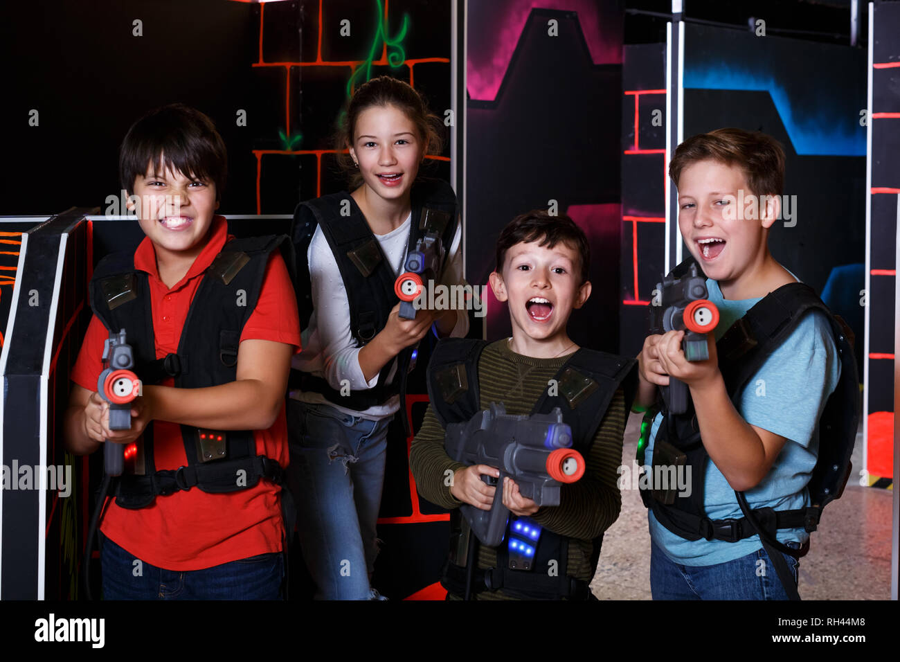 Smiling kids with laser pistols posing together in dark laser tag ...