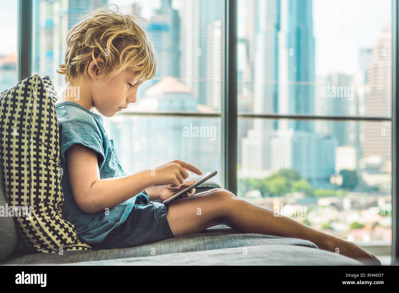 Boy uses a tablet at home on the couch in the background of a window ...