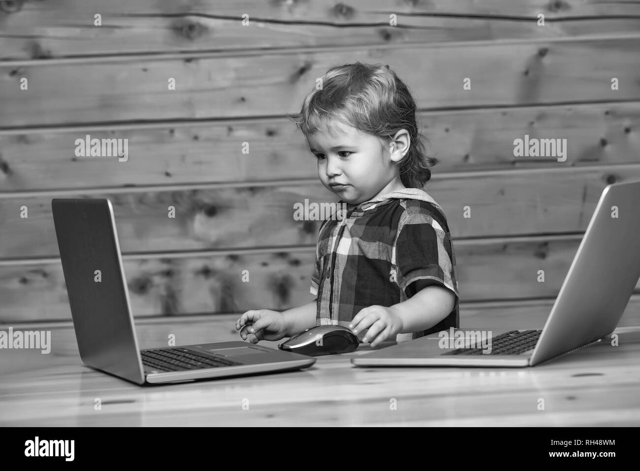 Cute baby boy child with blond curly hair plays on two laptop computers ...
