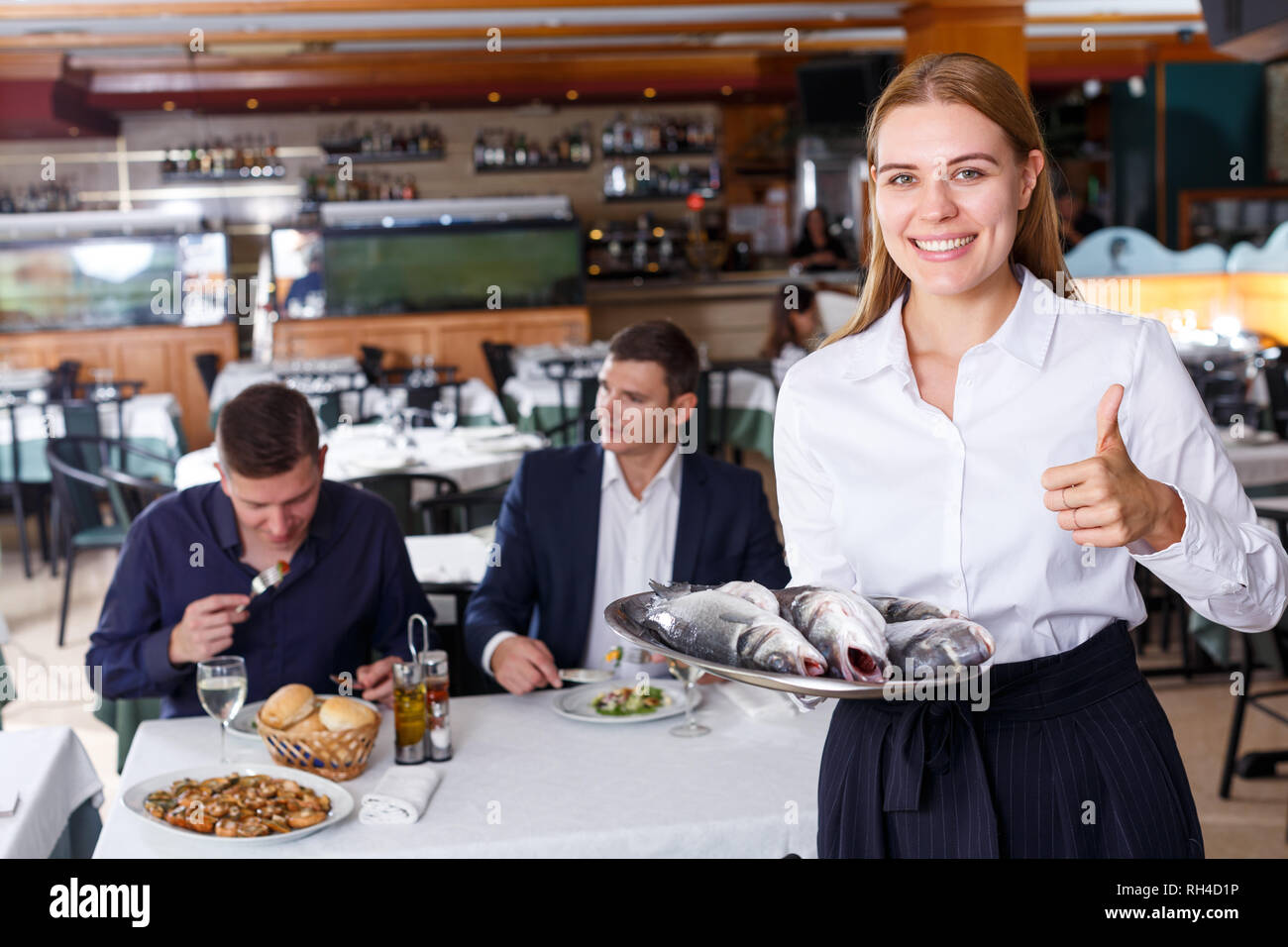 Waitress in white shirt demonstrating tray of fish serving for two male ...