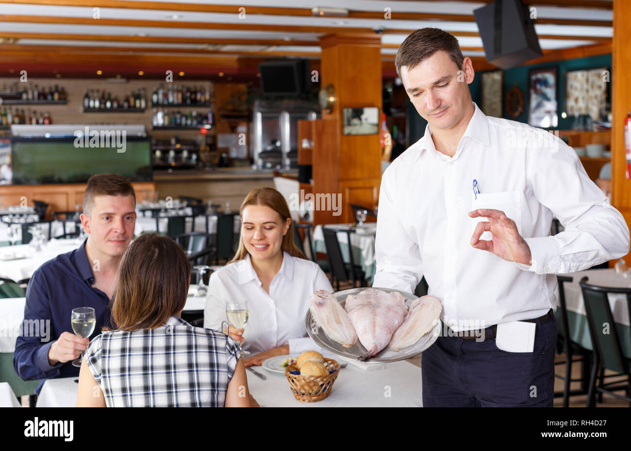 Waiter in white shirt showing tray of fish serving for group of ...