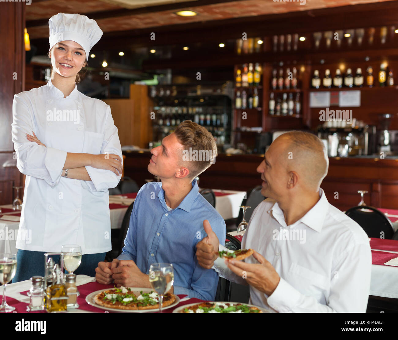 Delighted guests lauding young female chef while enjoying pizza in cozy ...