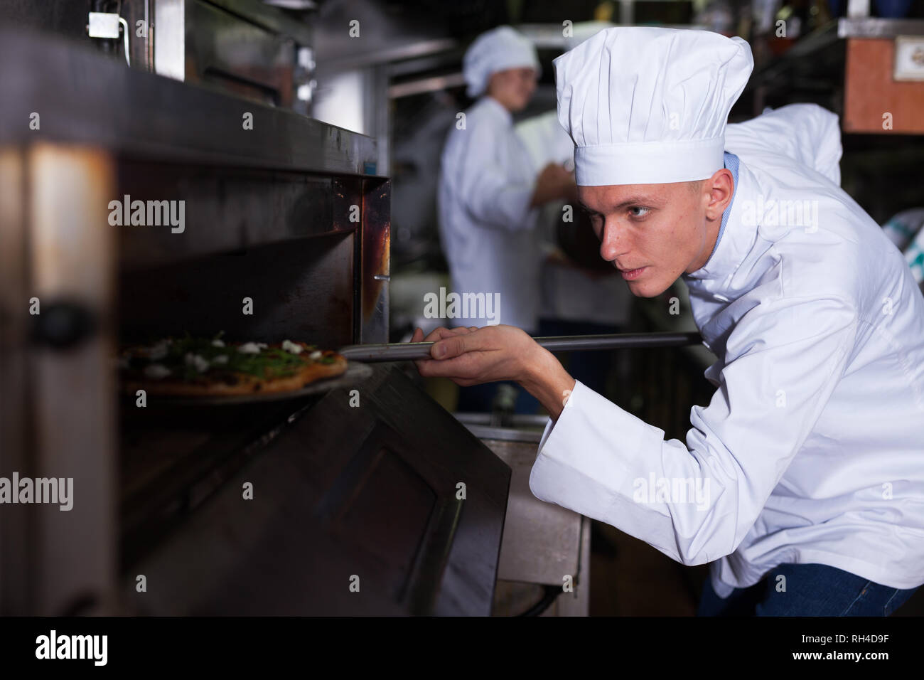 Portrait of confident young chef working in modern restaurant kitchen ...