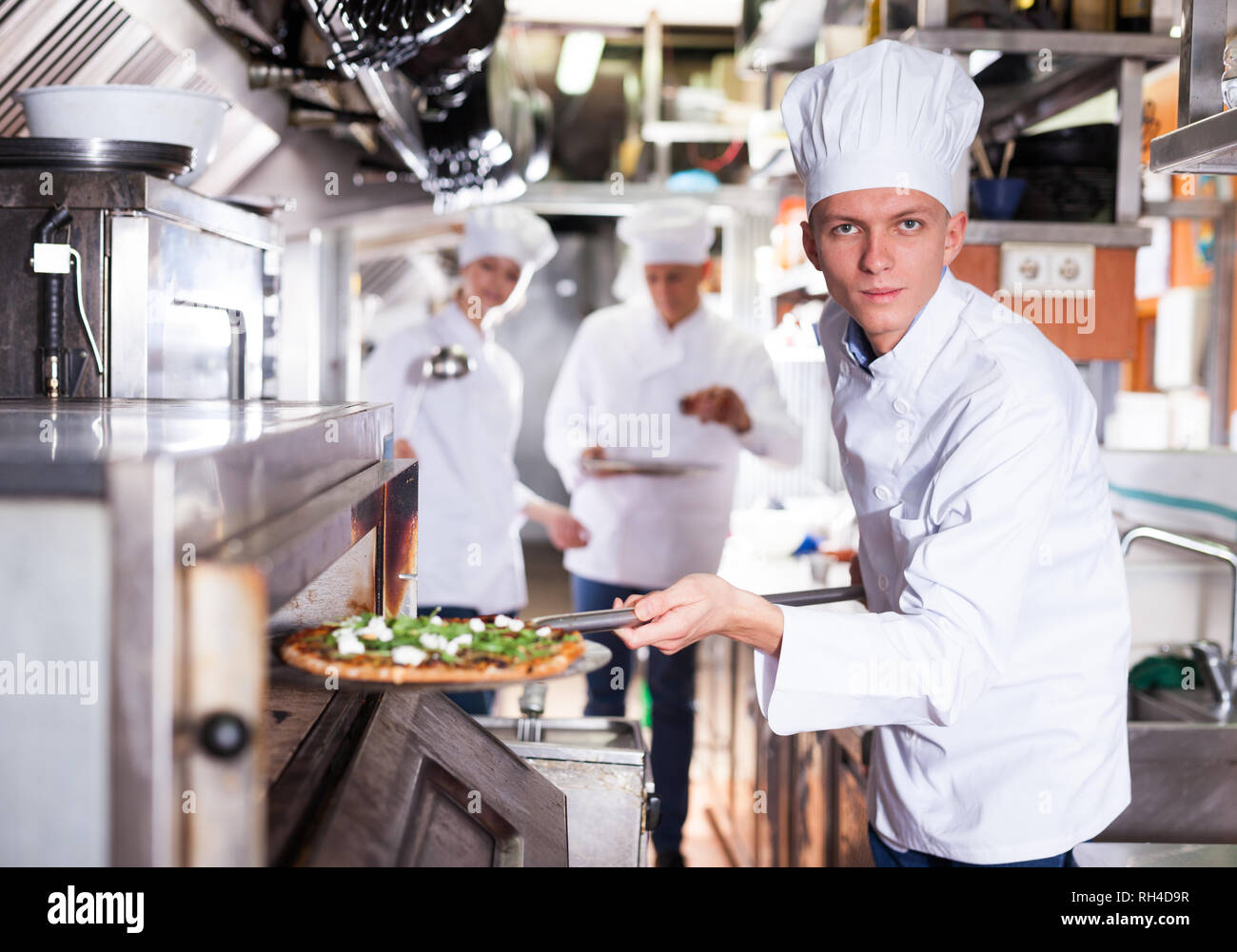 Portrait of confident young chef working in modern restaurant kitchen ...