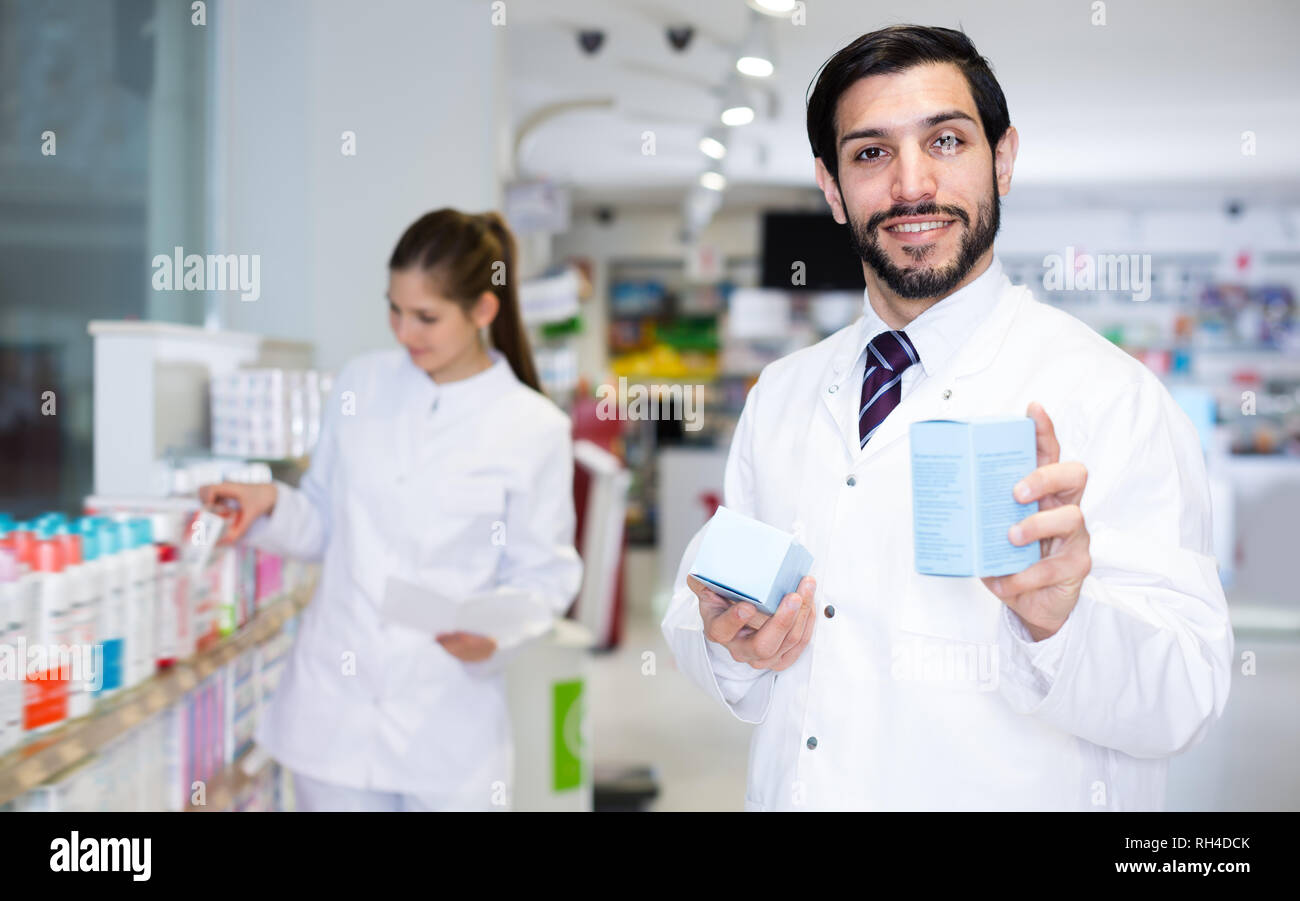 Nice male specialist who is holding medicines near shelves in pharmacy ...