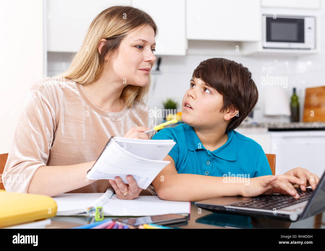 Woman helping tweenage boy with lessons sitting together at home ...