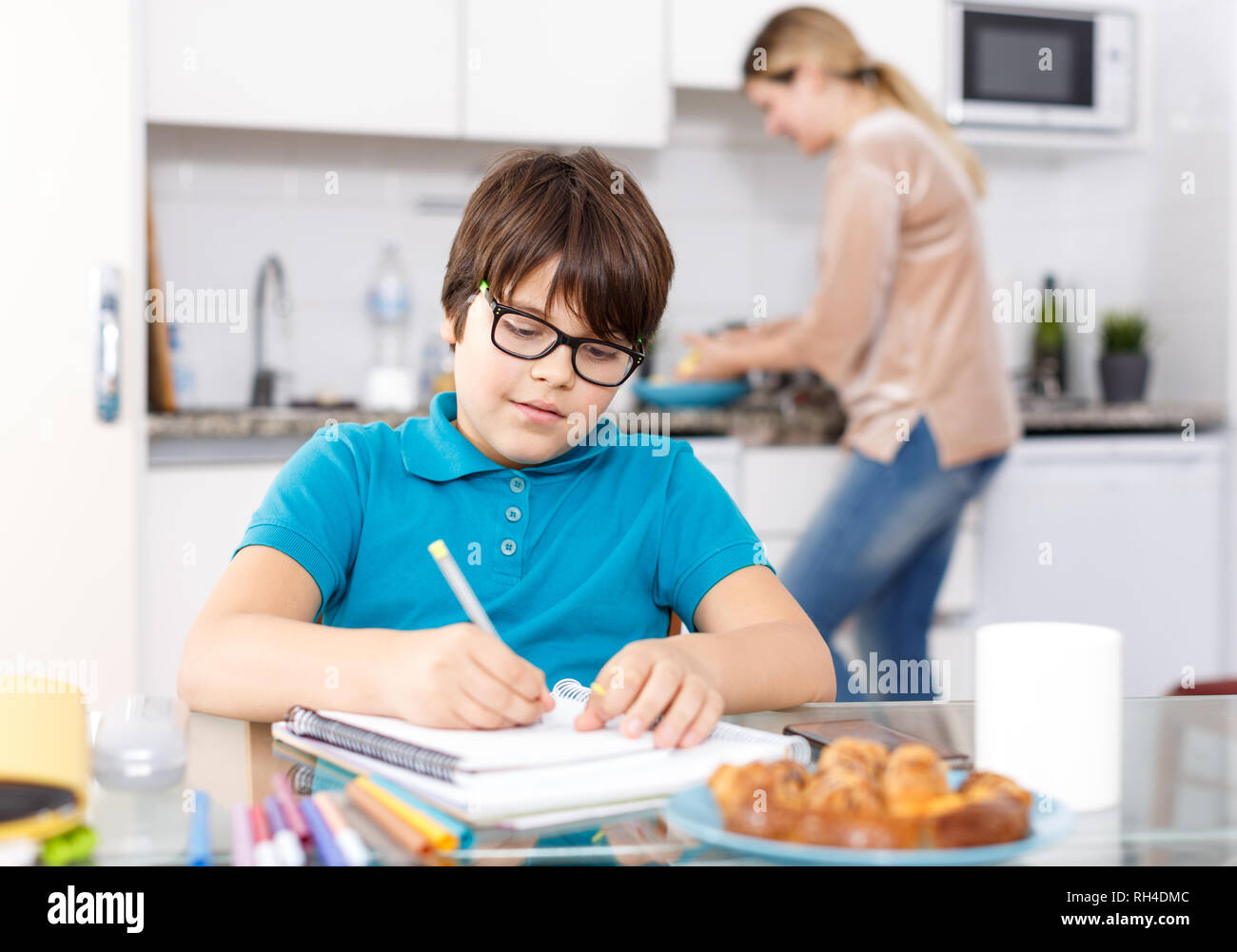 Portrait of boy studying at kitchen table and doing homework while his ...