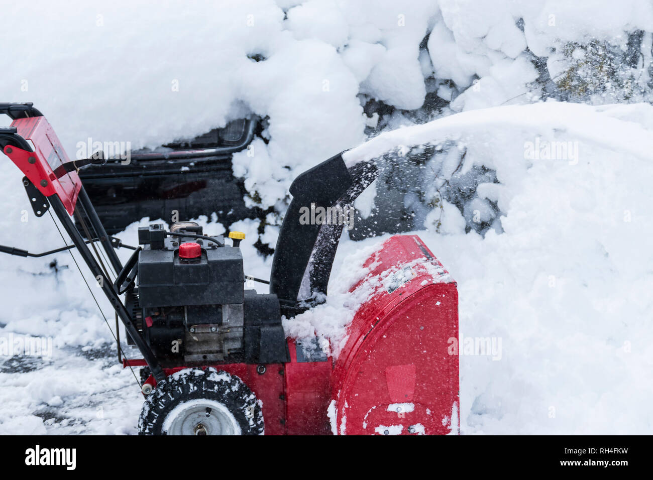 A close up of a red snow blower shooting snow across a driveway after a ...