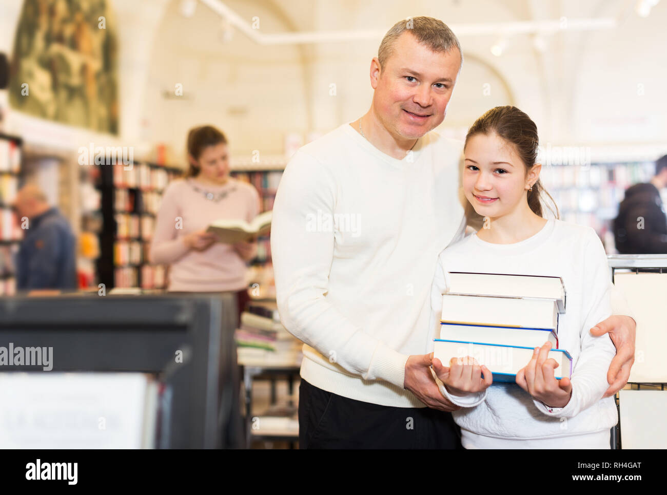 Positive little girl with her loving father holding pile of books ...