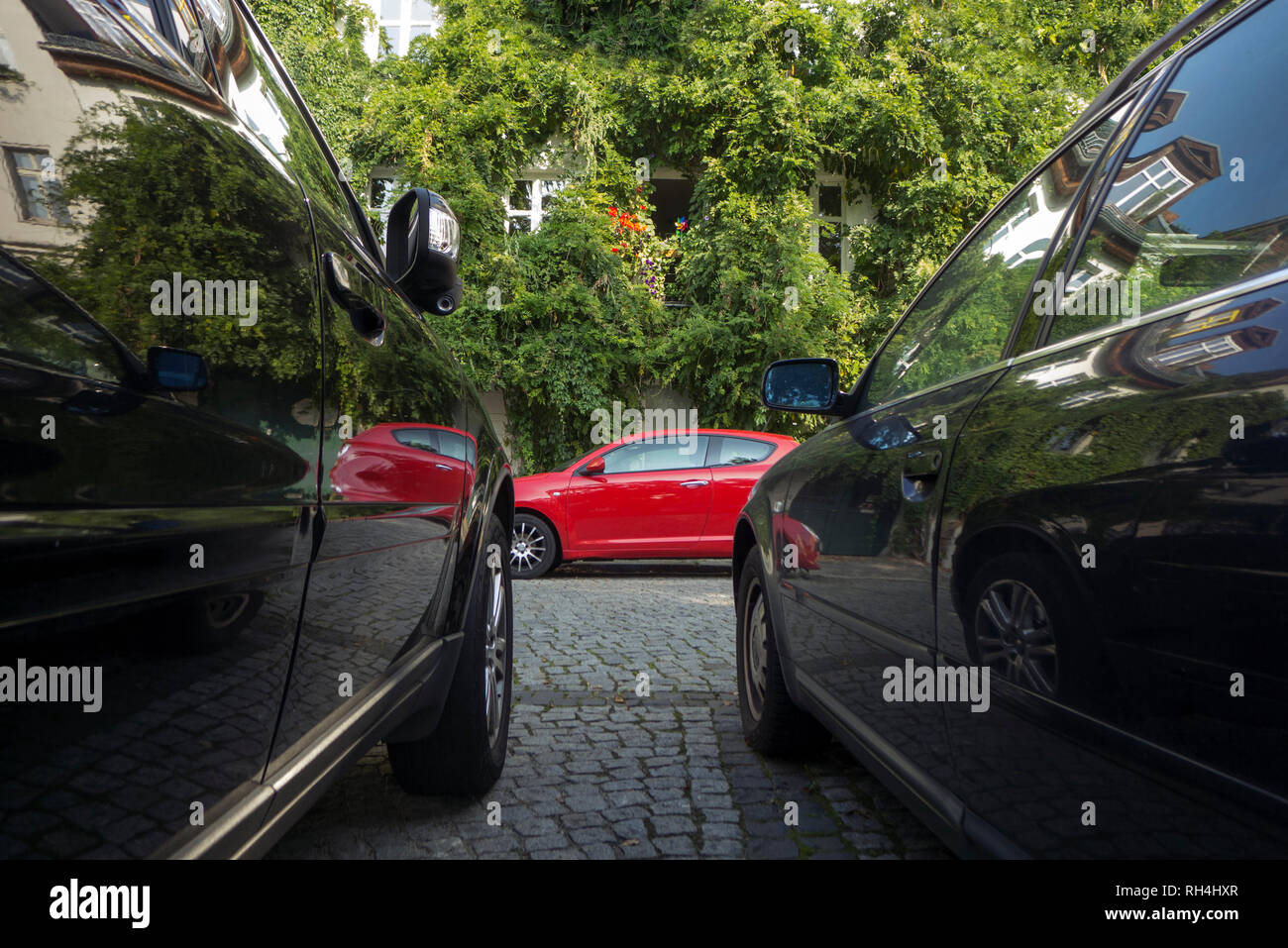 Cars against ivy covered building. Red car view in gap between black ...