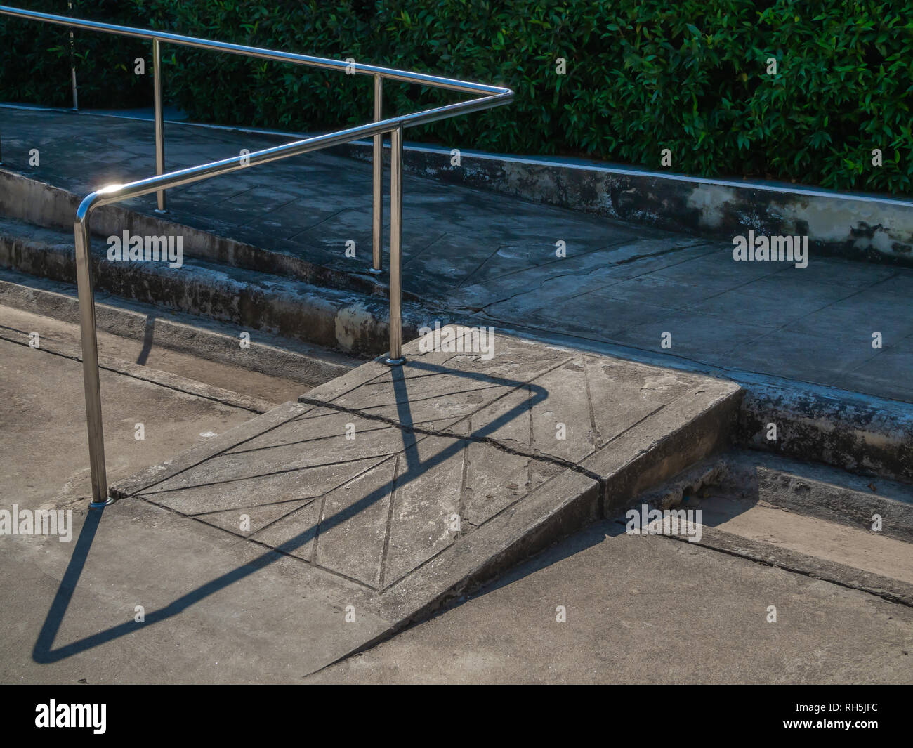 Old grunge wheelchair ramp with metal bar on green bush background ...