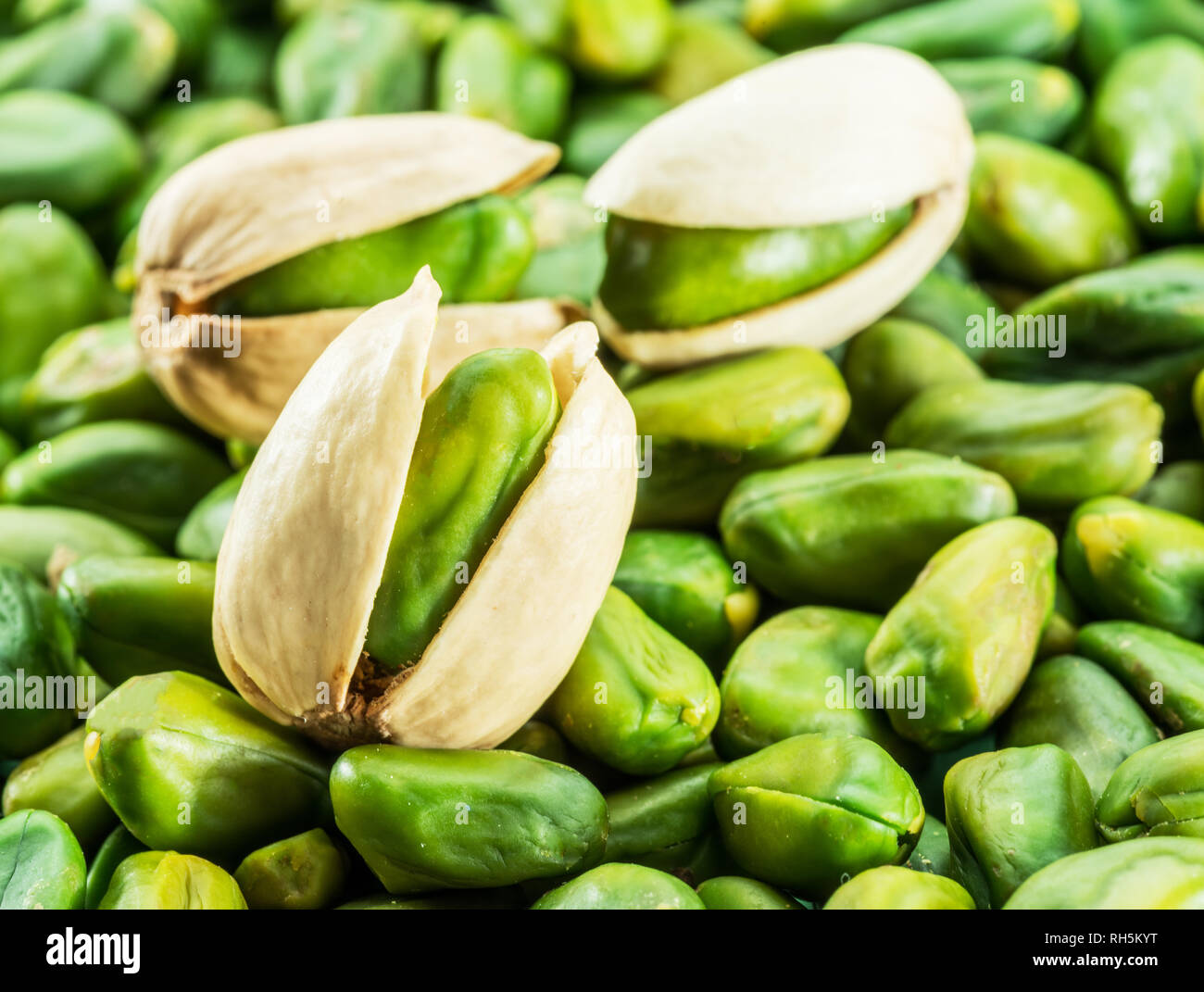 Green pistachio nut with shell over lot of pistachios. Food background ...