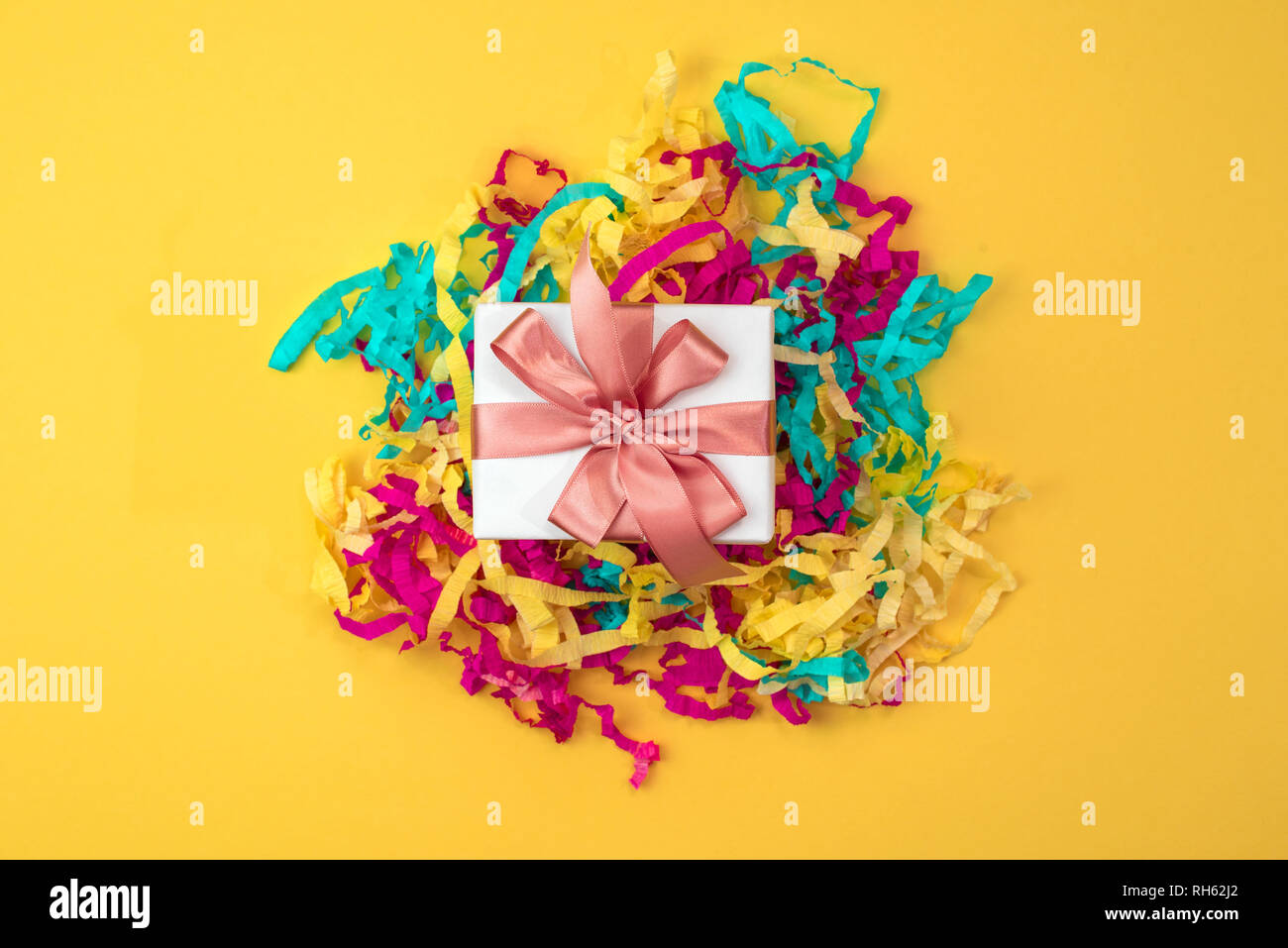 Gift box with colored streamers bright yellow background. A top view of ...