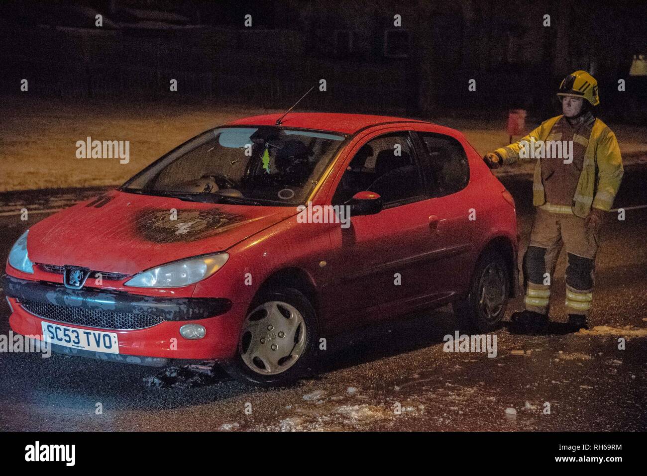 A member of the Fire Service is seen standing next to the car with fire ...