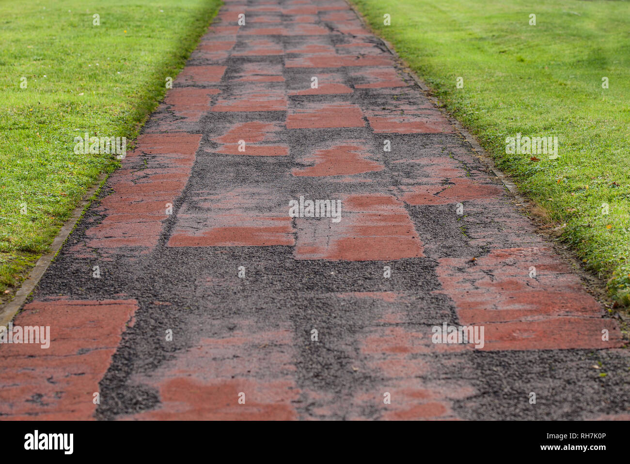 Red tarmac pathway weathered. Bordered by grass Stock Photo - Alamy