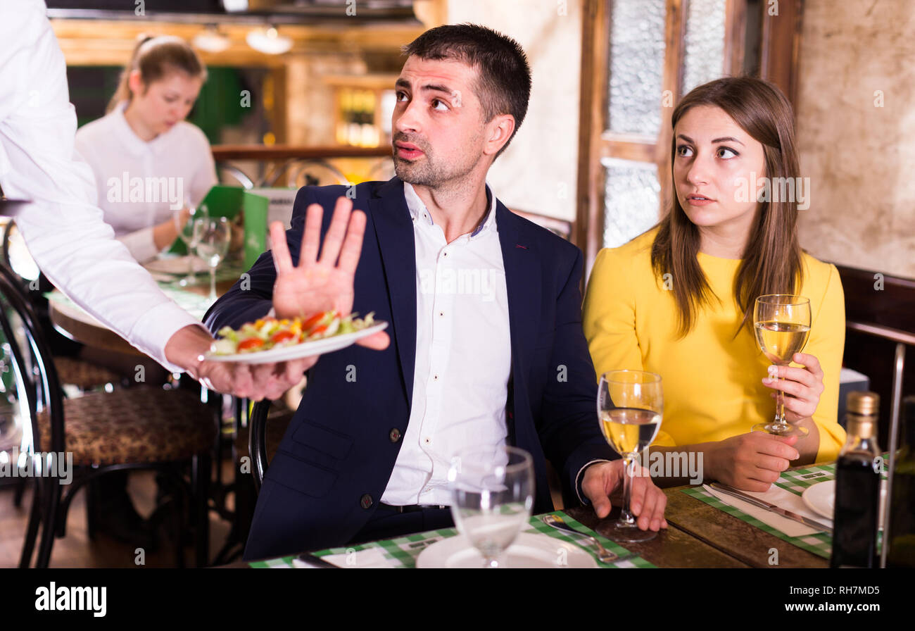 Portrait of dissatisfied couple who is dining and refusing salad in ...