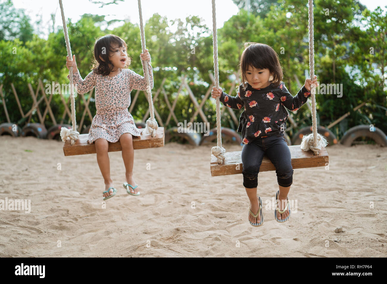 togetherness of the two sisters when playing a swing at the playground ...