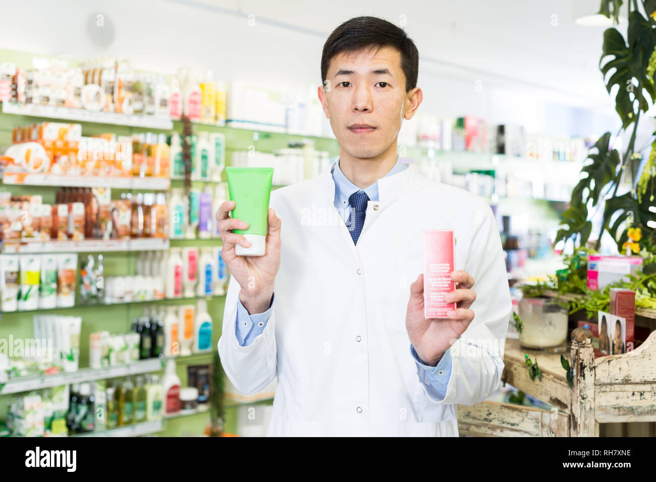 Smiling chinese man pharmacist is standing with medicines in pharmacy ...