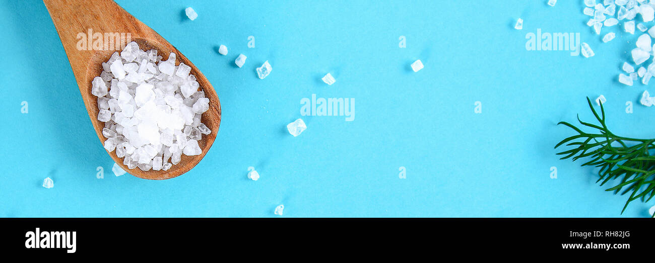 Crystals of large sea salt in a wooden spoon and dill on a blue table ...