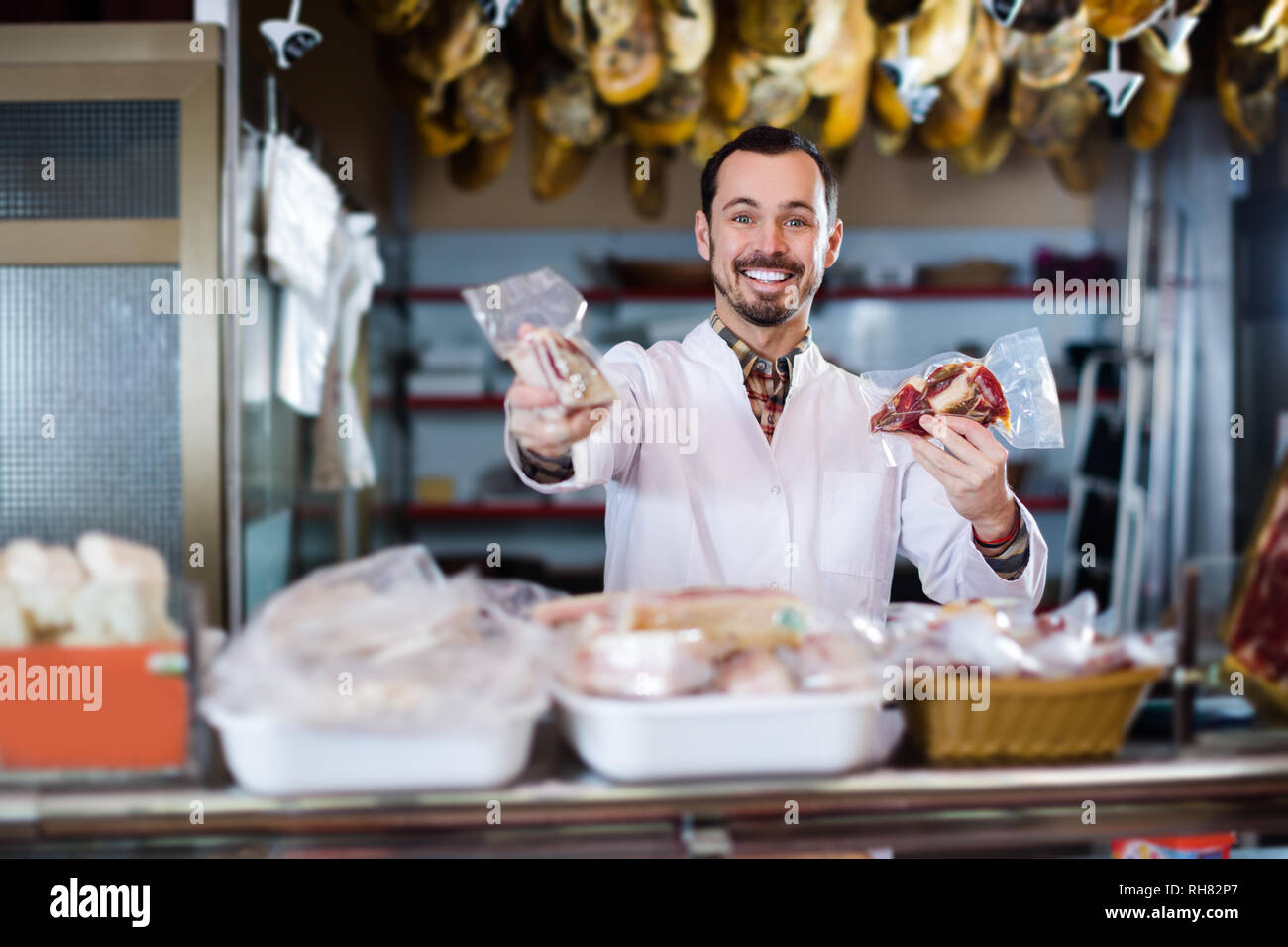 Positive male seller showing sorts of meat in butcher’s store Stock ...