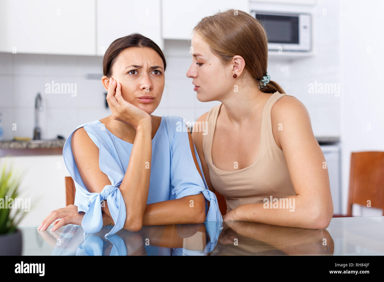 Girl telling her frustrated female friend bad news in kitchen interior ...