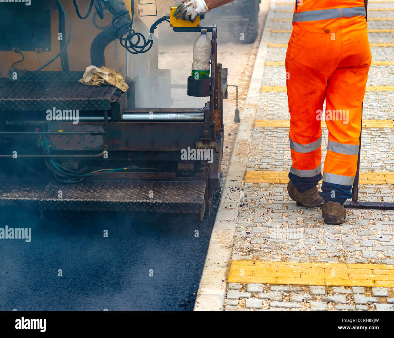 Workers regulate tracked paver laying asphalt heated to temperatures ...