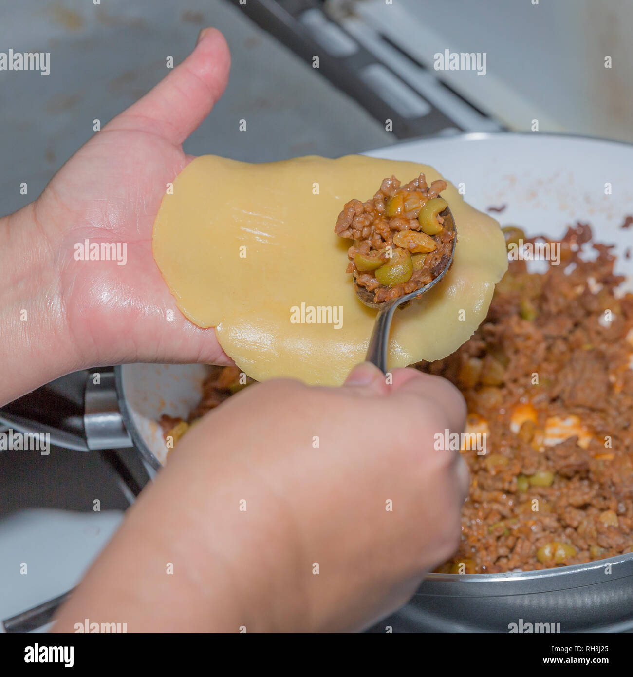 image of female hands spooning ground beef prepared with olives onto ...