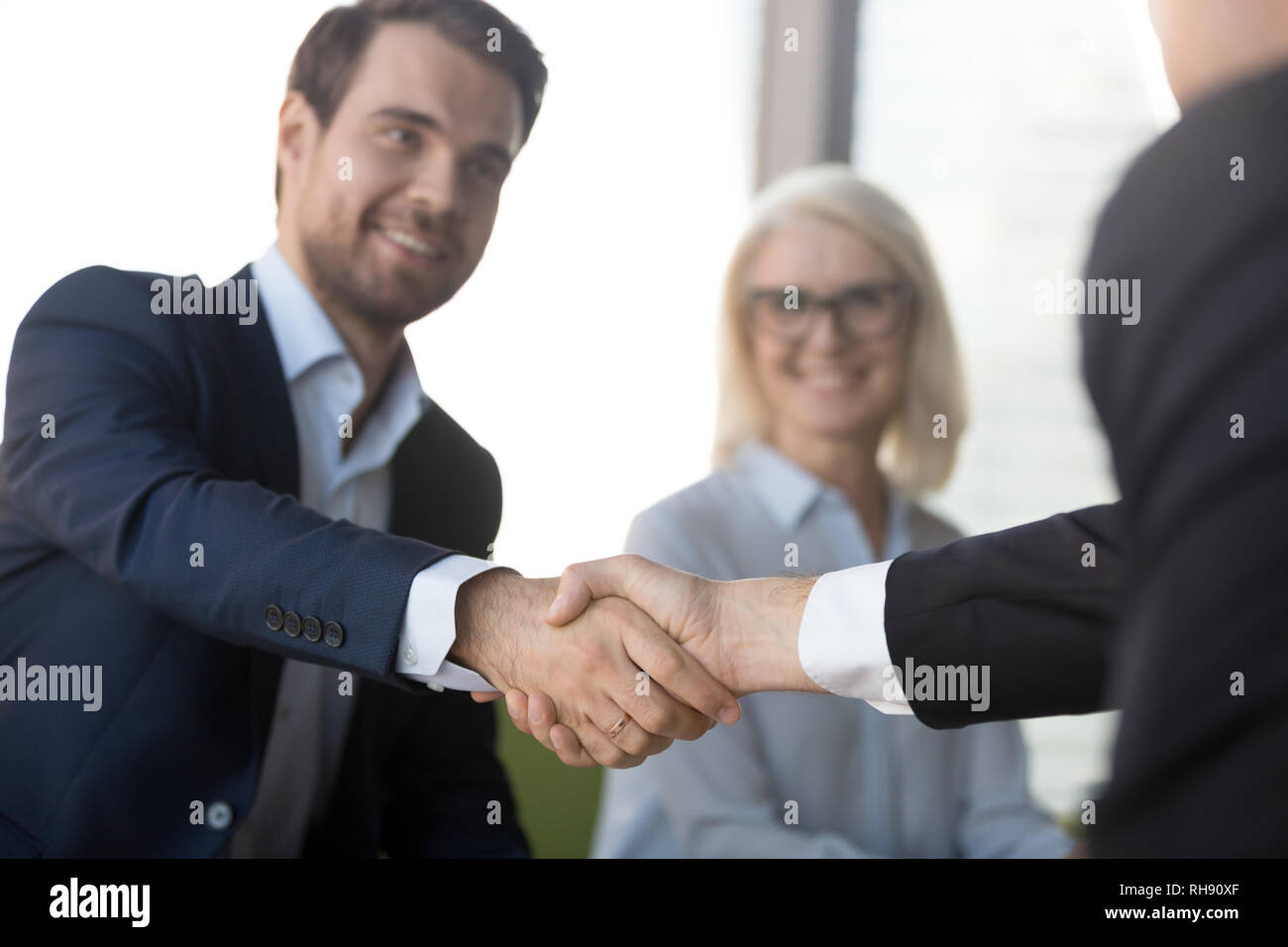 Smiling successful businessmen in suits shaking hands expressing ...