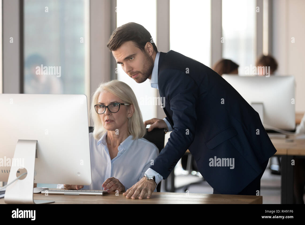 Serious male mentor supervising female employee helping with computer ...