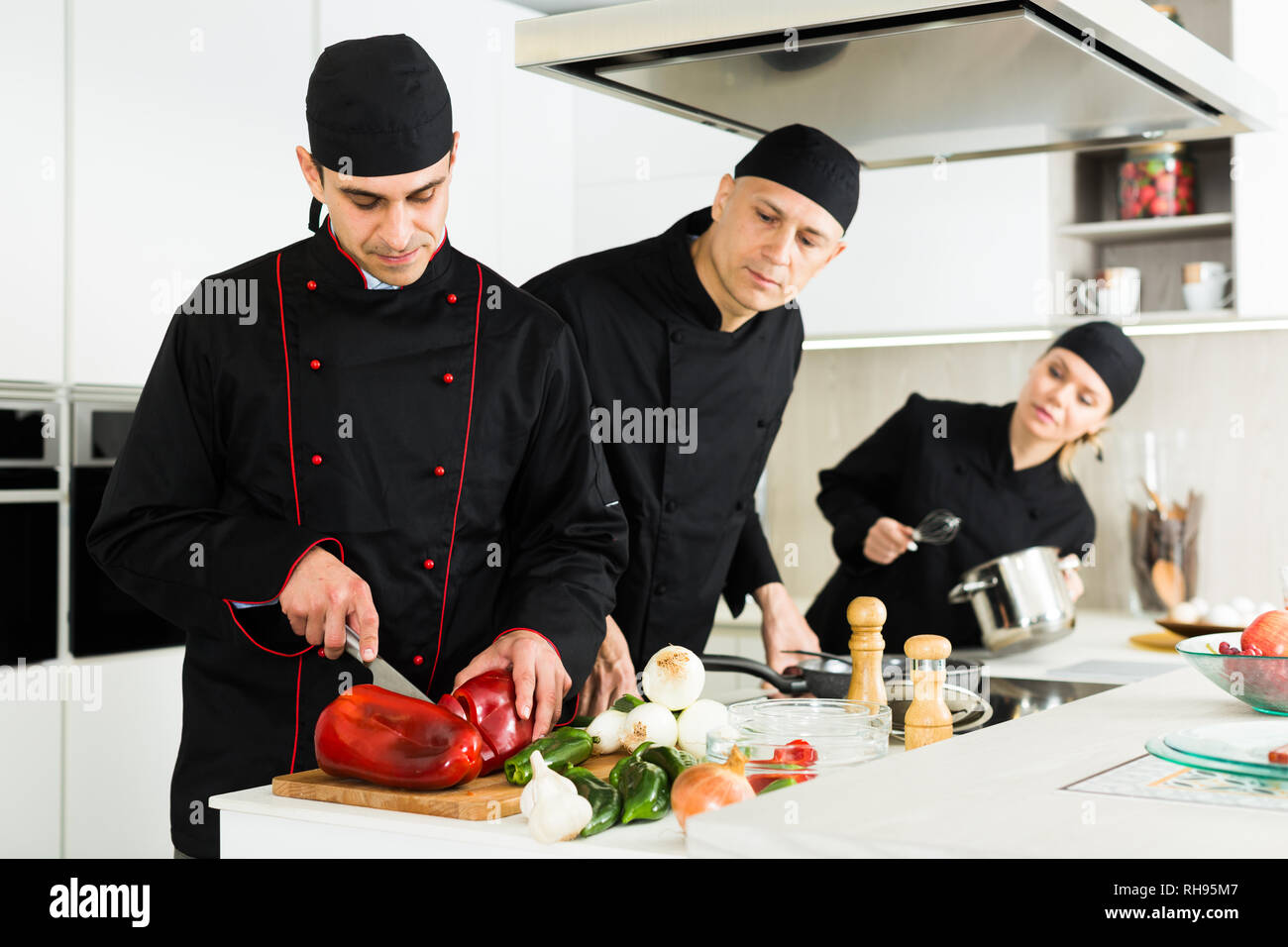 Female and two male cooks are making salad on their work place in the ...