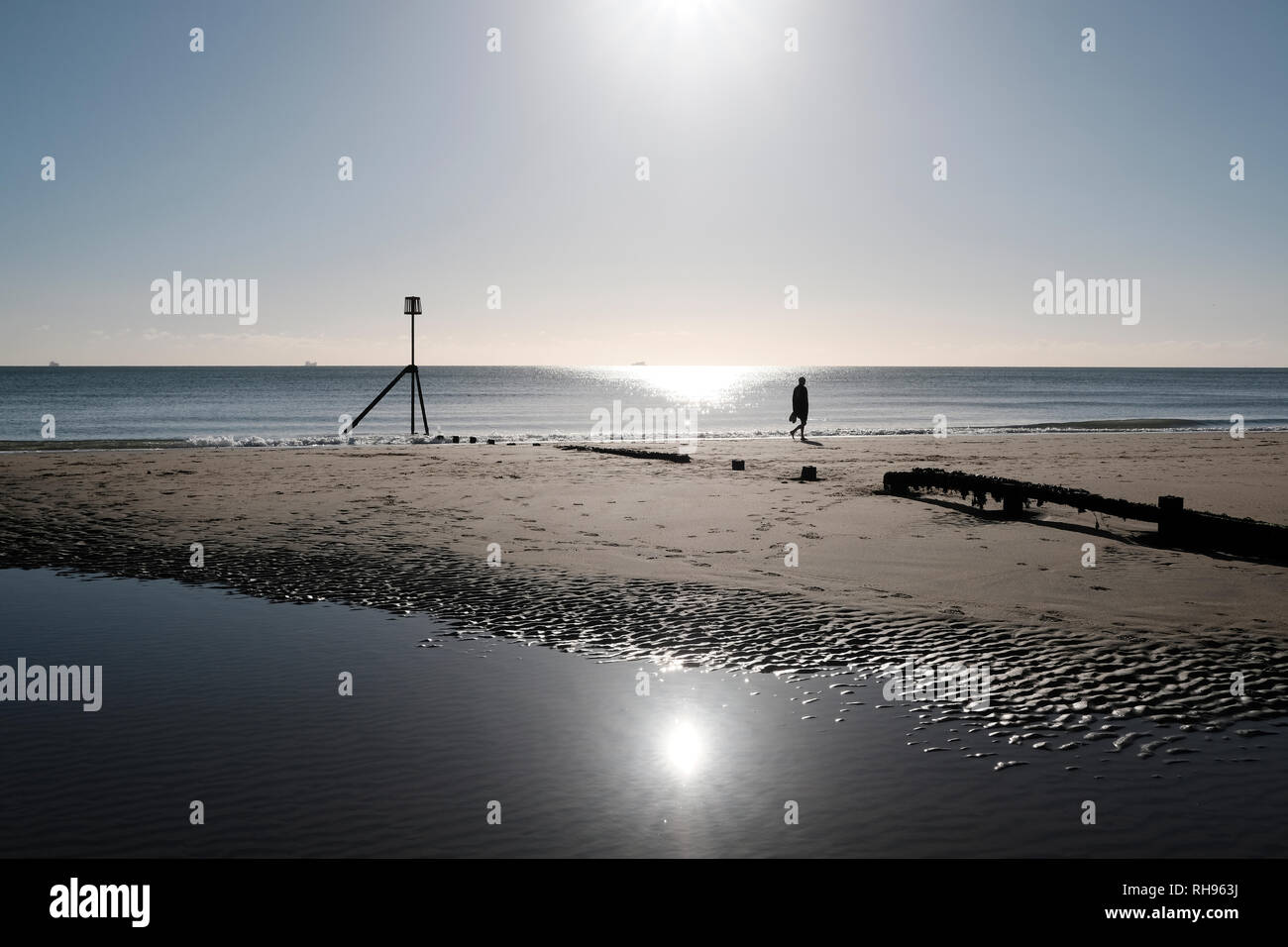A lone walker, carrying his shoes, walking along Sandown seafront beach ...