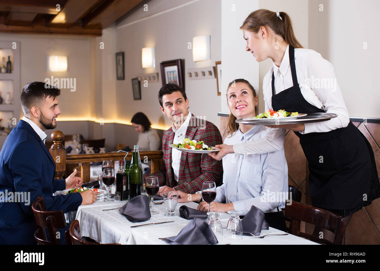 Attractive waitress serving meals to friendly company at restaurant ...