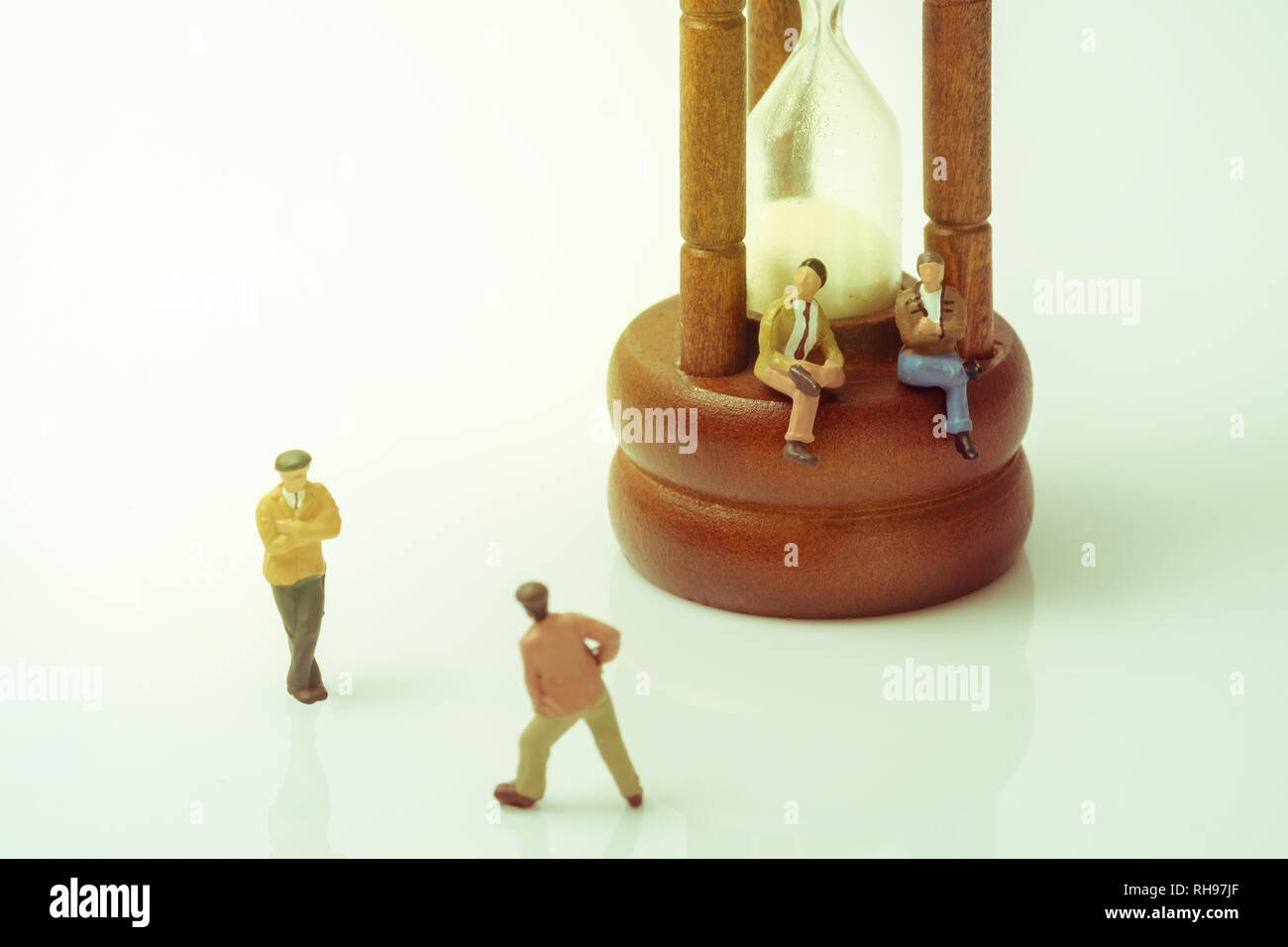 View of miniature toy people with vintage hourglass on white background ...