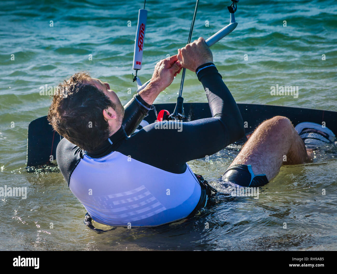 A kitesurfer leans back in his harness and positions his feet on his ...
