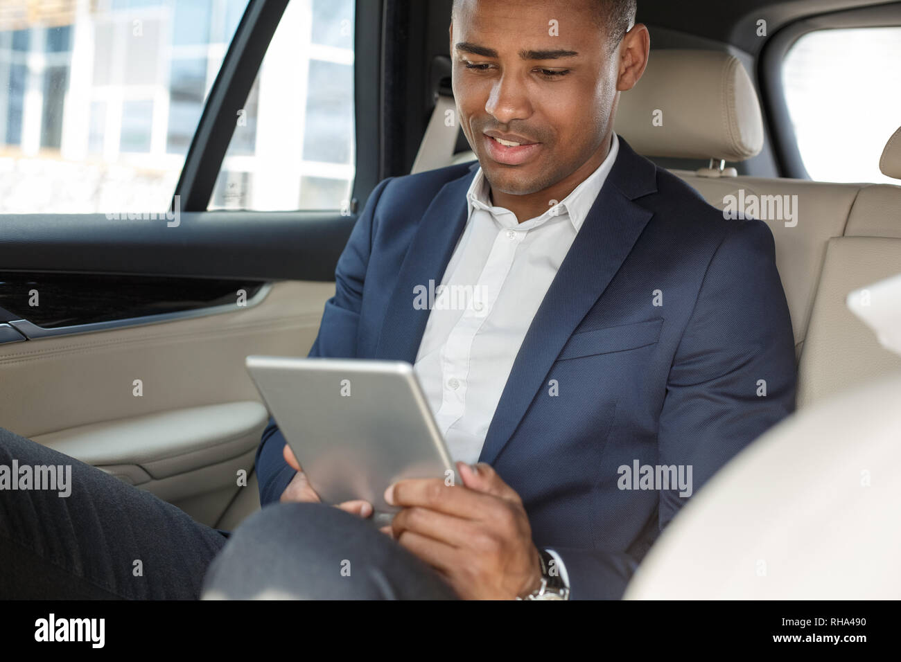 Young mulatto businessman sitting on the back seat in the car watching ...