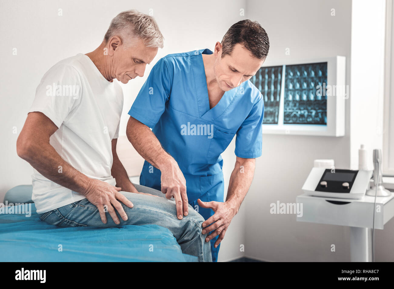 Dark-haired doctor wearing blue uniform examining knee Stock Photo - Alamy