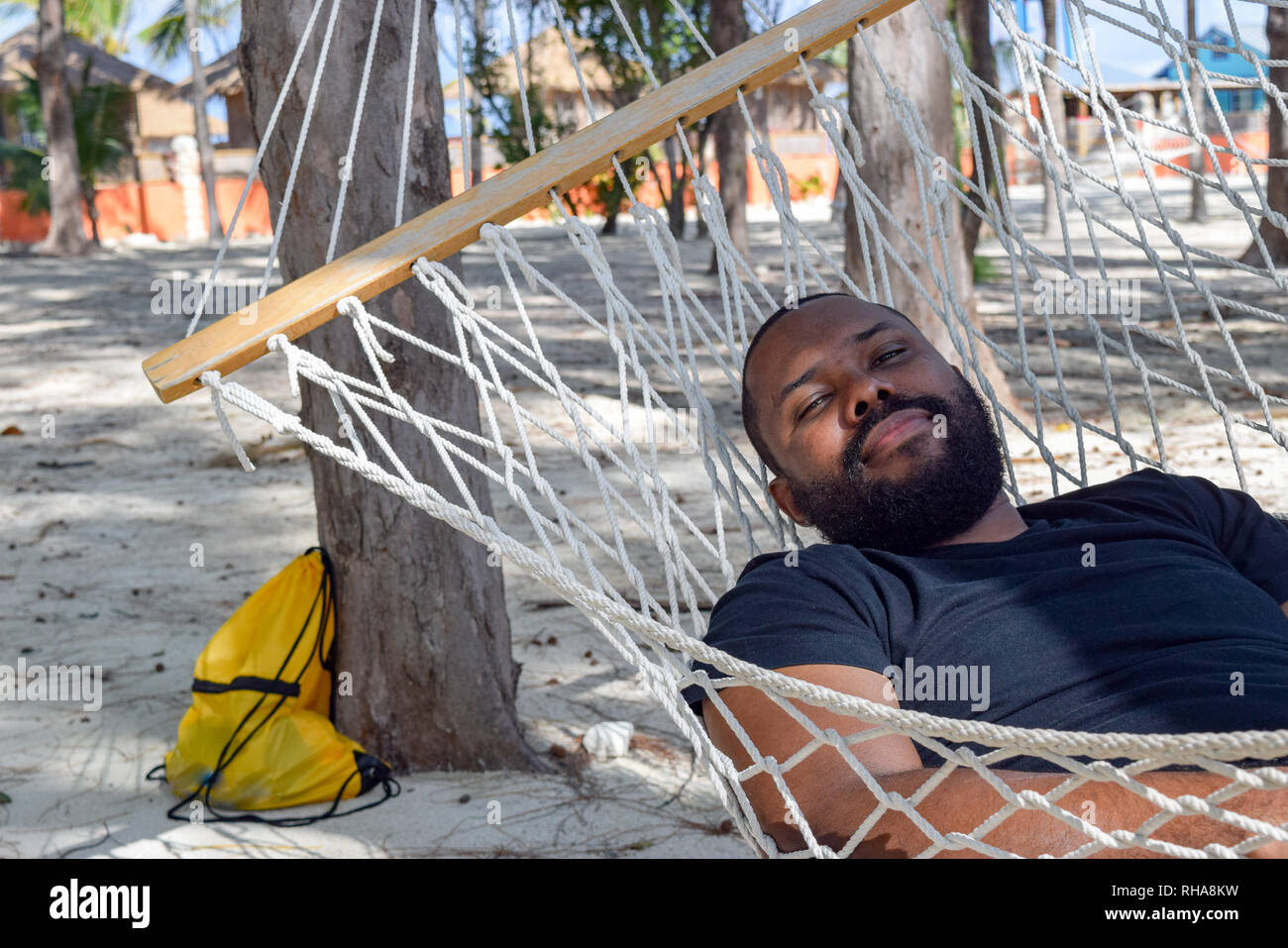 Black male mid 40s lying in hammock on tropical beach wearing black ...