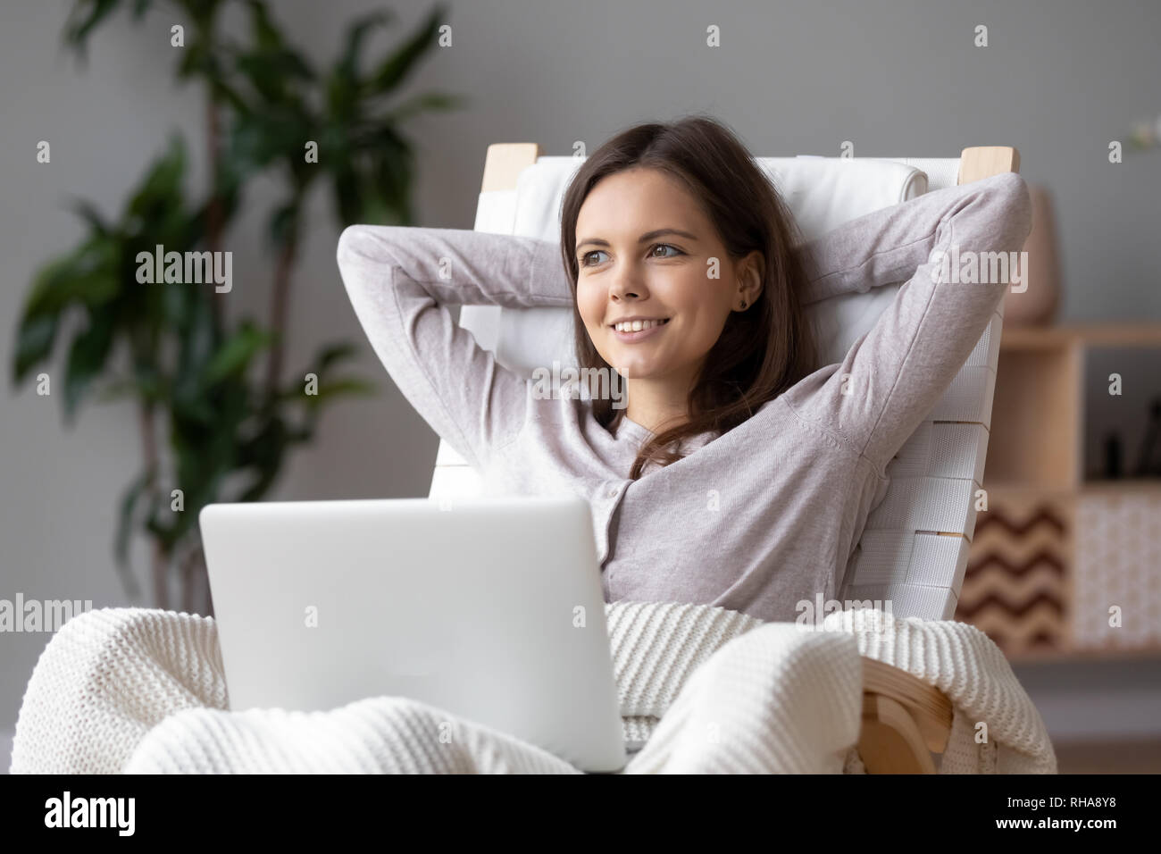 Happy young woman resting on chair at home with laptop Stock Photo - Alamy